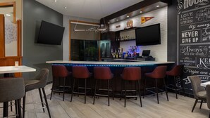 Uma área de bar moderna com balcão, banquetas e uma parede com frases inspiradoras.