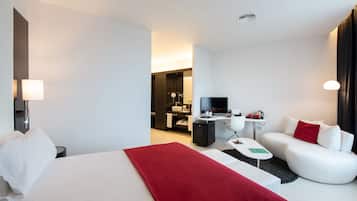 Quarto de hotel moderno com uma cama grande, um sofá branco, uma pequena mesa e uma televisão.