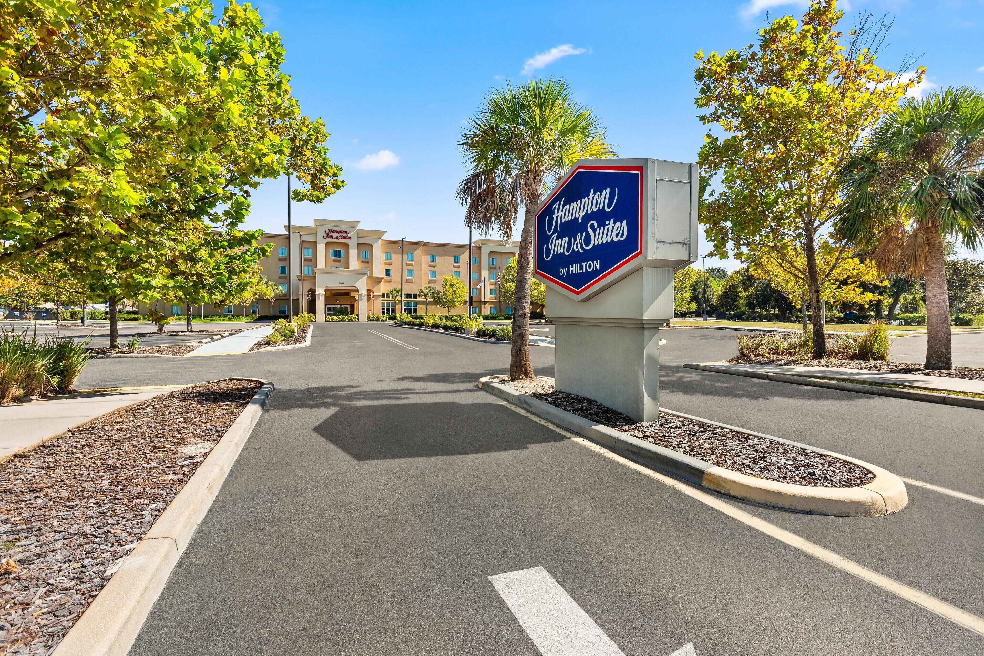 Placa da Hampton Inn & Suites em frente a um edifício com estacionamento e árvores.