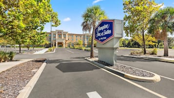 Placa da Hampton Inn & Suites em frente a um edifício com estacionamento e árvores.