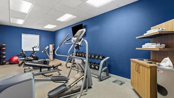Uma academia com máquinas de cardio, halteres e uma pequena área de cozinha.