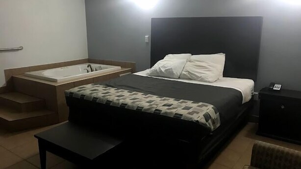 Quarto com cama, mesa de cabeceira, pequeno criado-mudo e uma banheira integrada.