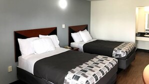Duas camas de solteiro com cabeceiras de madeira, paredes cinzentas e uma pequena mesa de cabeceira com uma luminária.
