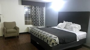Quarto com cama, cadeira, janela com cortinas e luminária fixada na parede.