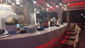 Uma área de bar com balcão, diversas garrafas e um espaço para sentar com cadeiras.