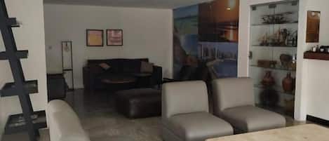 Uma sala de estar com sofá, poltronas, mesa de centro e estante de livros.