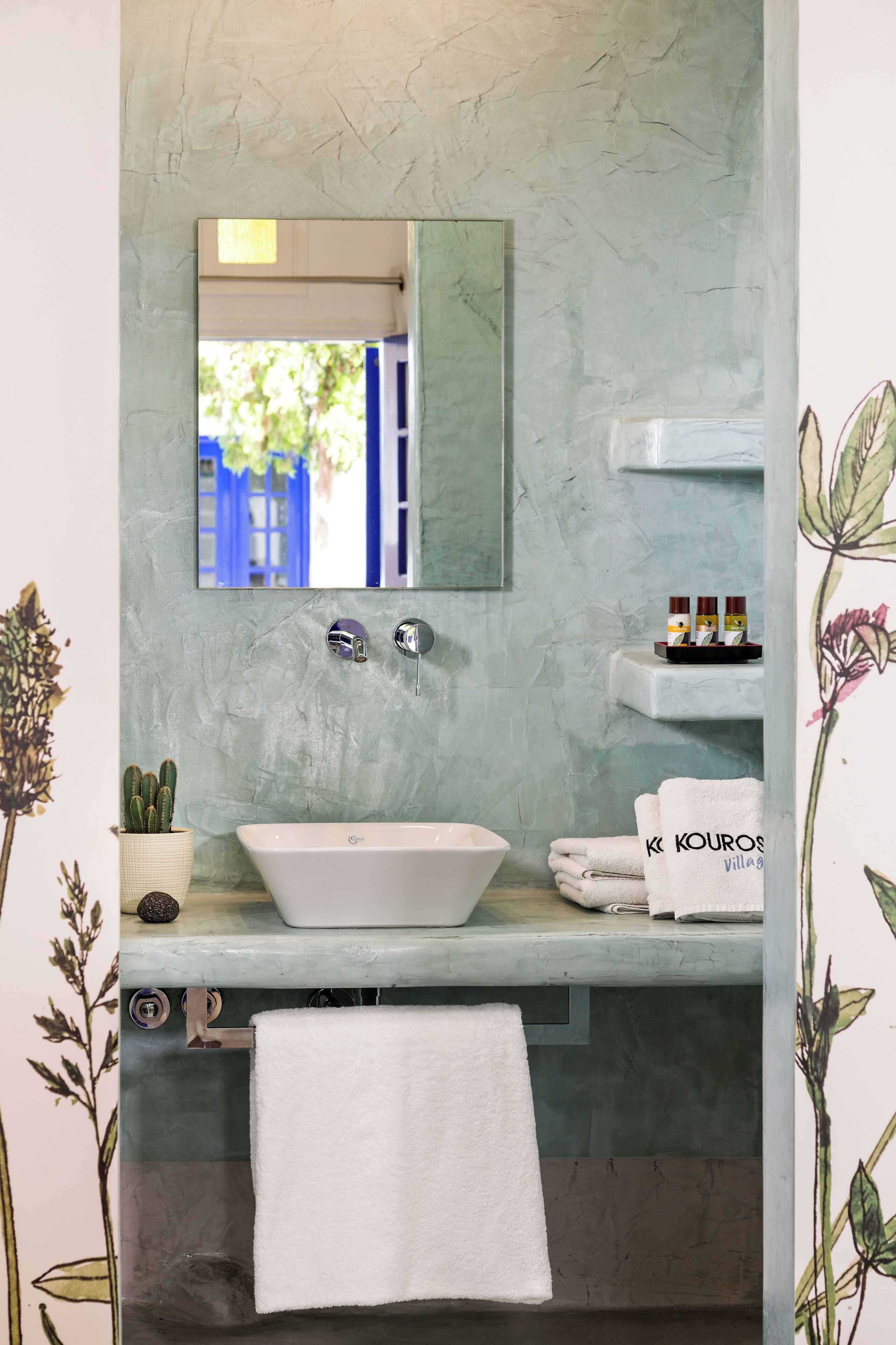 Casa de banho com lavatório branco, espelho, porta-toalhas e prateleira com produtos de higiene pessoal.