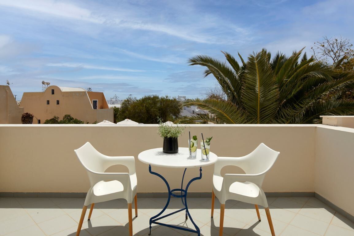 Um terraço no telhado com uma mesa redonda e duas cadeiras brancas, uma planta em vaso e duas bebidas sobre a mesa.