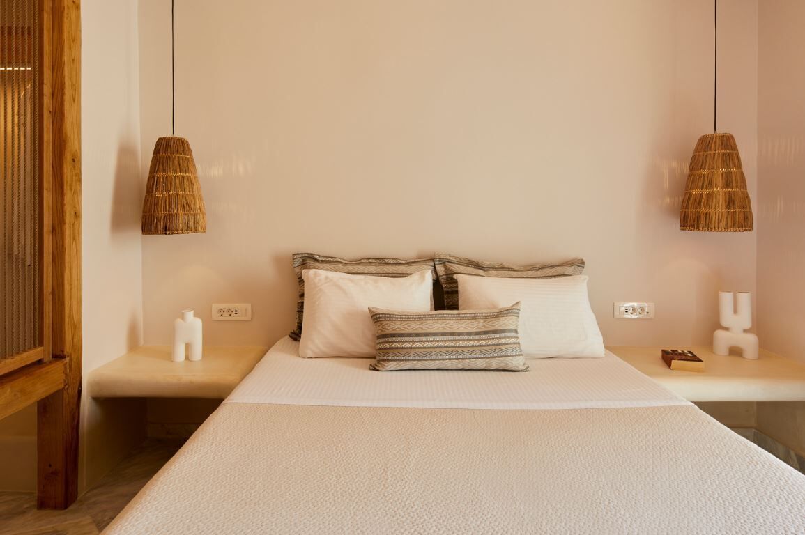 Quarto bem arrumado com cama, almofadas, mesas de cabeceira e luminárias pendentes.