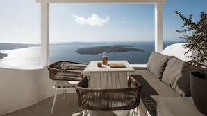 Um terraço com cadeiras de vime e uma mesa, com vista para a paisagem marítima e ilhas.