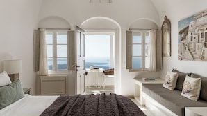 Quarto com uma cama grande, um sofá e vista para o mar através de portas abertas.