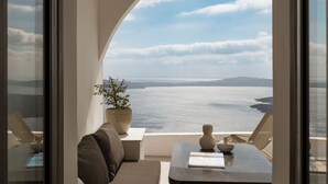 Uma varanda com vista para o mar, um vaso de planta, uma mesa com uma tigela e um livro, e um sofá.