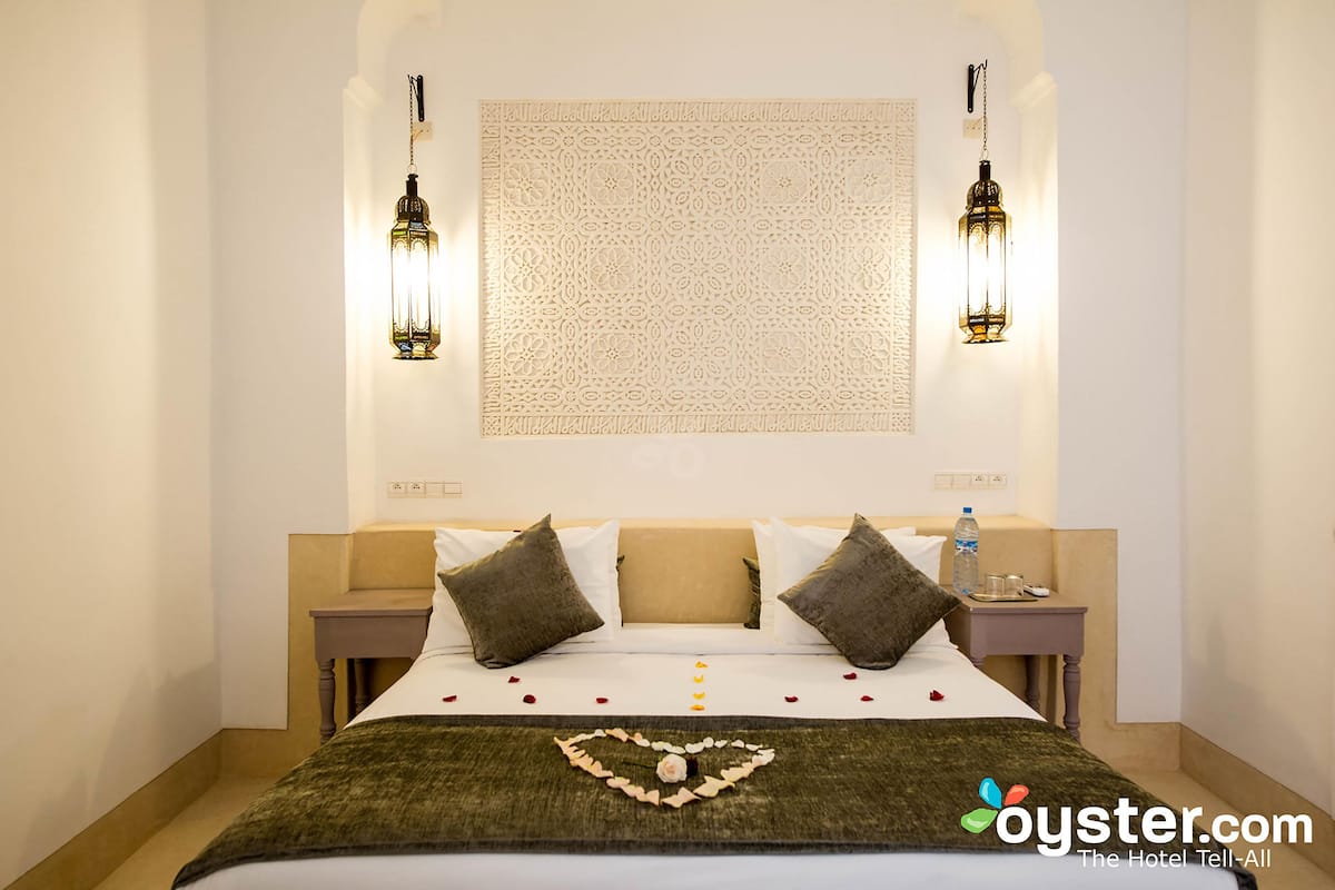 Quarto de hotel com cama bem arrumada, duas mesas de cabeceira, um painel decorativo na parede e duas luminárias de parede.