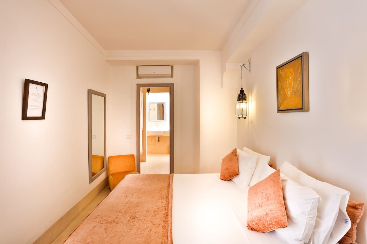 Quarto de hotel com cama, espelho, quadro emoldurado e luminária na parede.