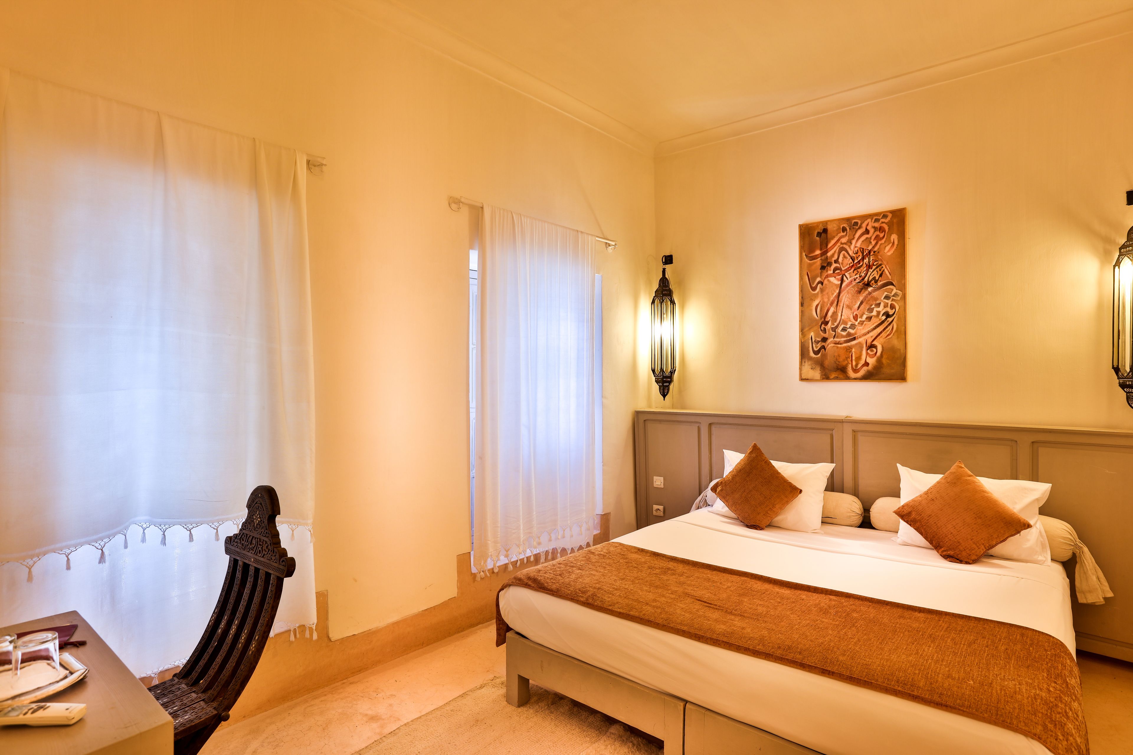 Quarto de hotel com cama, uma cadeira, uma mesa e um painel decorativo na parede.