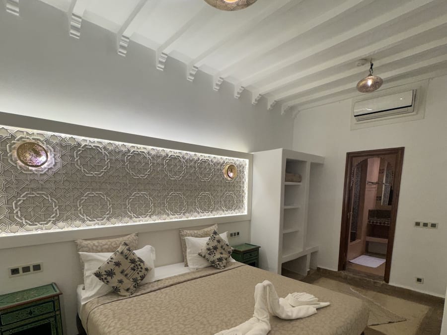 Um quarto com uma cama grande, um painel decorativo na parede, uma mesinha de cabeceira e um guarda-roupa.