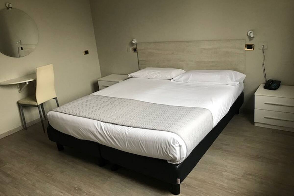 Quarto com cama, mesas de cabeceira, uma cadeira e escrivaninha.