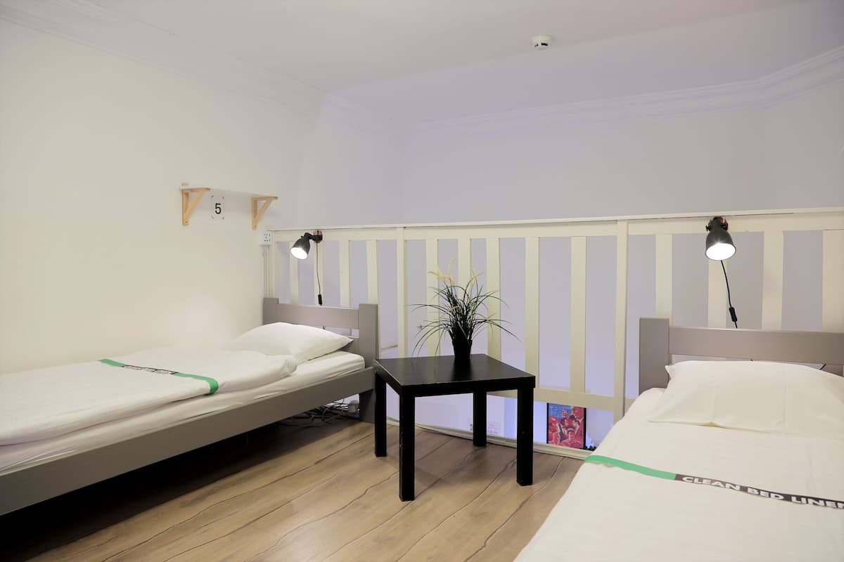 Quarto com duas camas de solteiro, uma pequena mesa com uma planta e um corrimão branco.