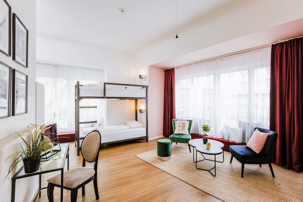Quarto moderno com beliche, mesa de jantar com cadeiras, poltrona verde e pequena mesa lateral.