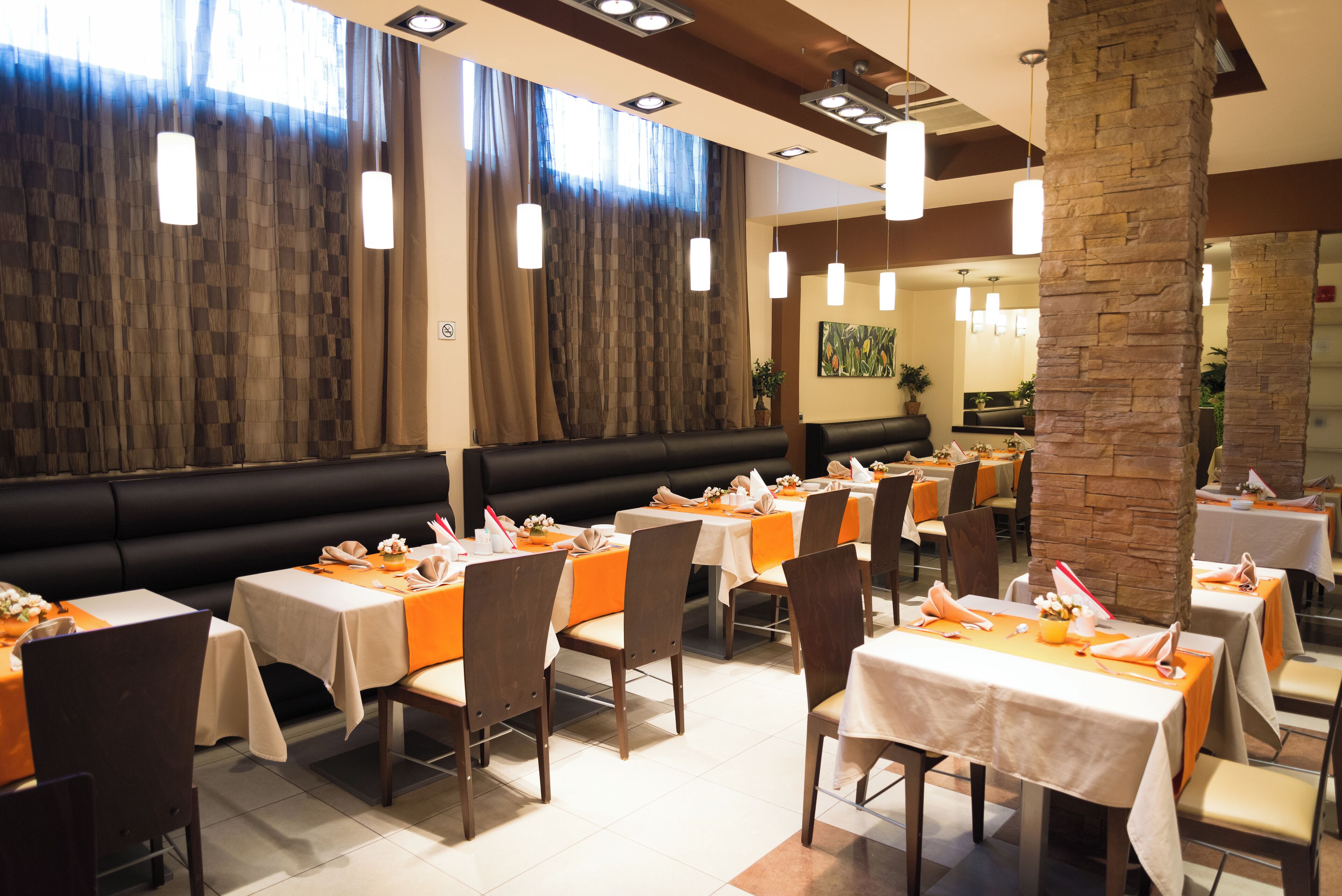 Um restaurante com várias mesas, cadeiras e uma janela grande com cortinas.