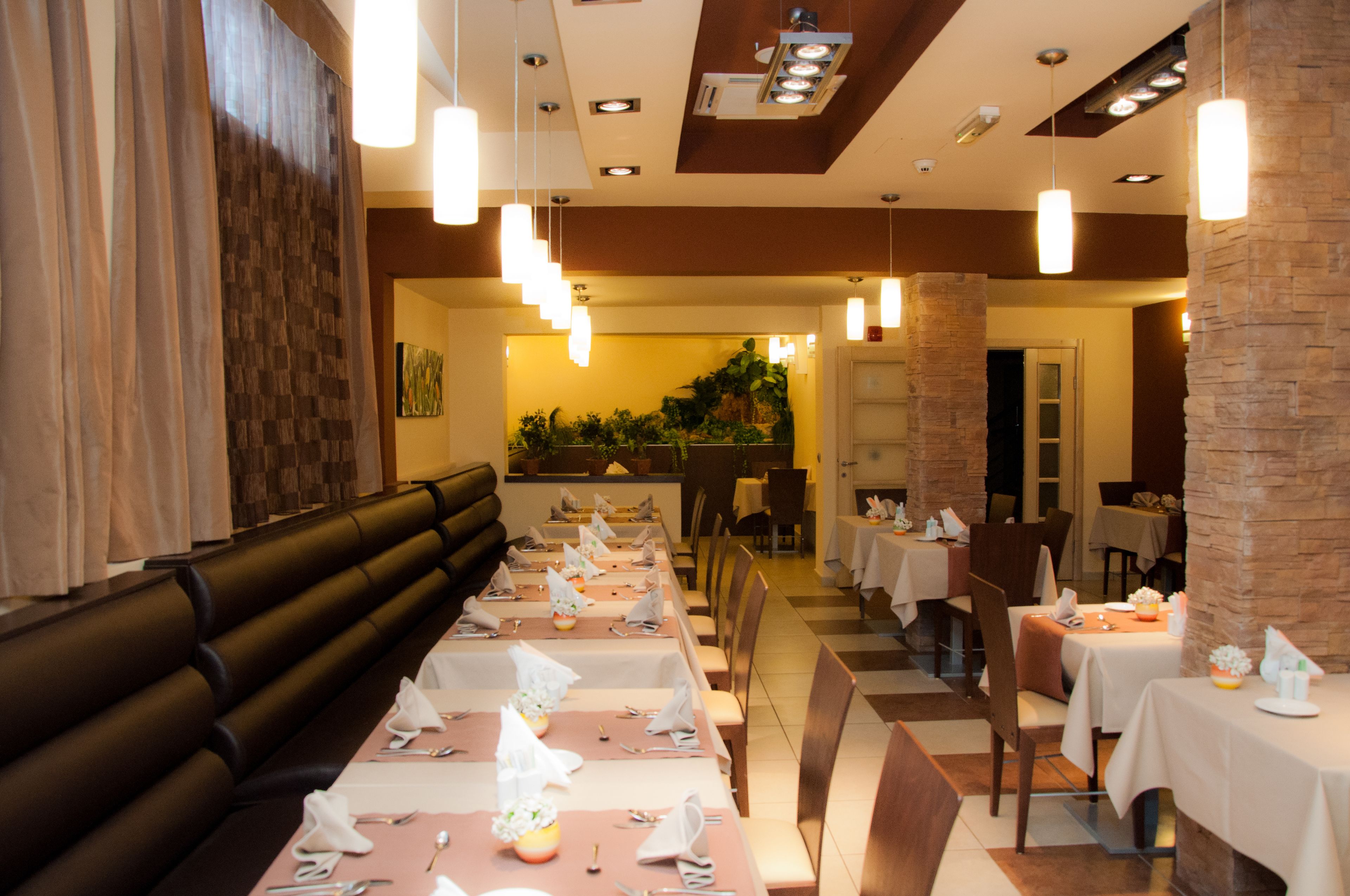 Um restaurante com mesas compridas preparadas para refeições, um bar e vista para a paisagem urbana.