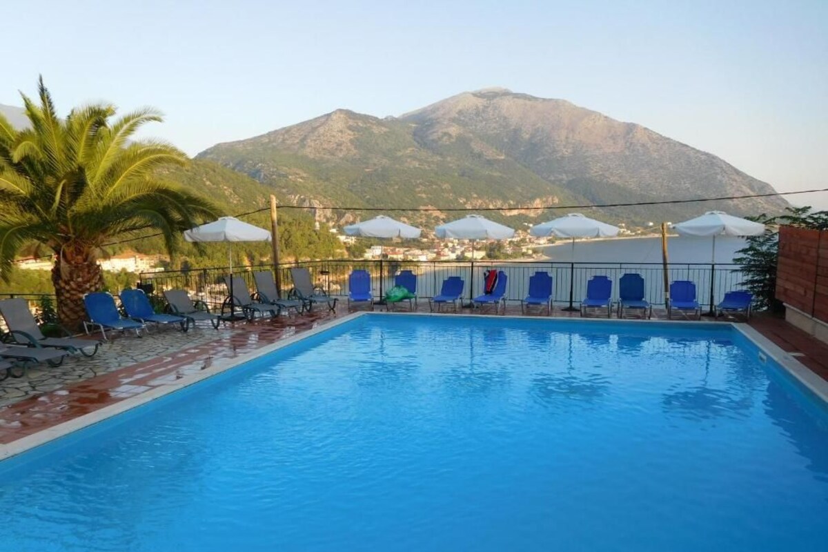 Uma piscina com espreguiçadeiras e guarda-sóis, uma palmeira e uma montanha ao fundo.