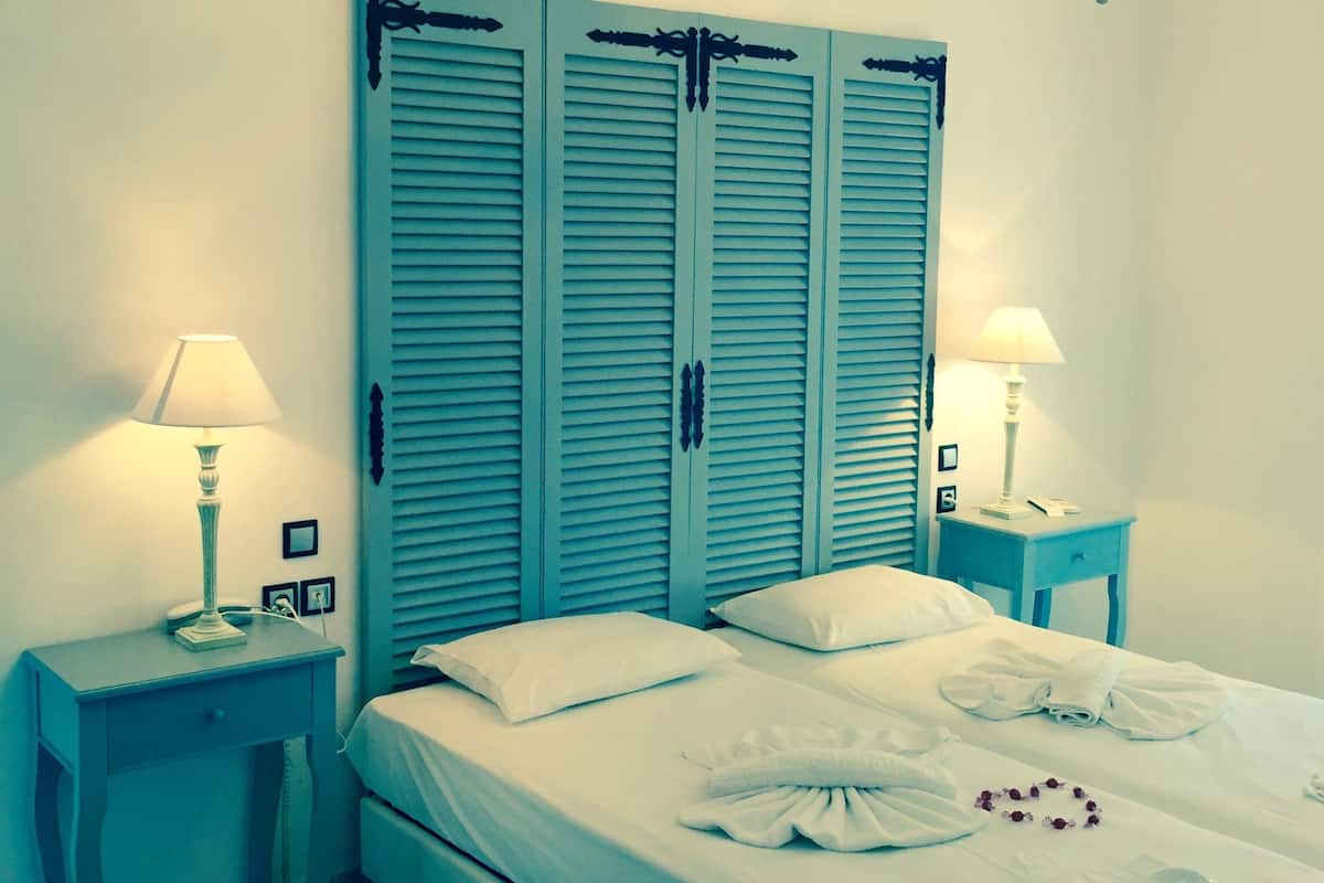 Quarto com cama, duas mesas de cabeceira com luminárias, um candelabro e um guarda-roupa com portas.
