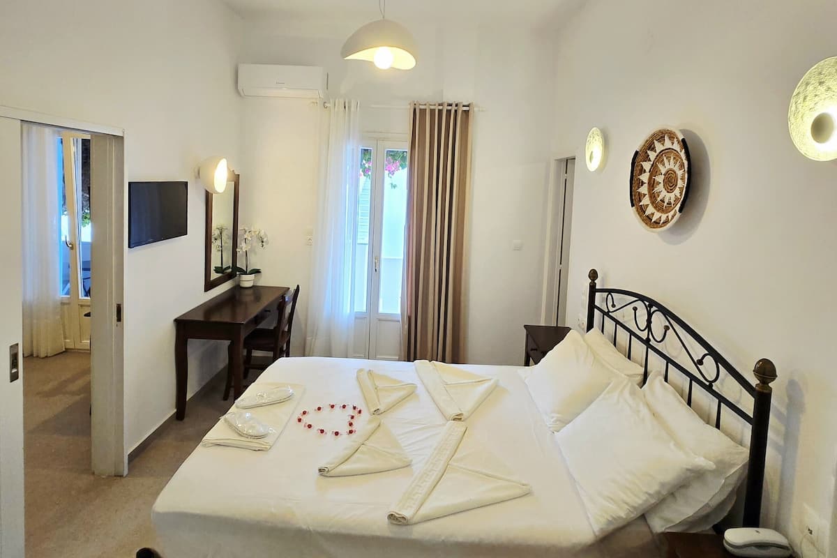 Quarto de hotel com cama, mesa de cabeceira, escrivaninha, cadeira, televisão e janela com cortinas.
