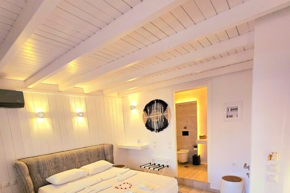 Quarto com uma cama grande, mesa de cabeceira, TV na parede e banheiro visível através de uma porta aberta.