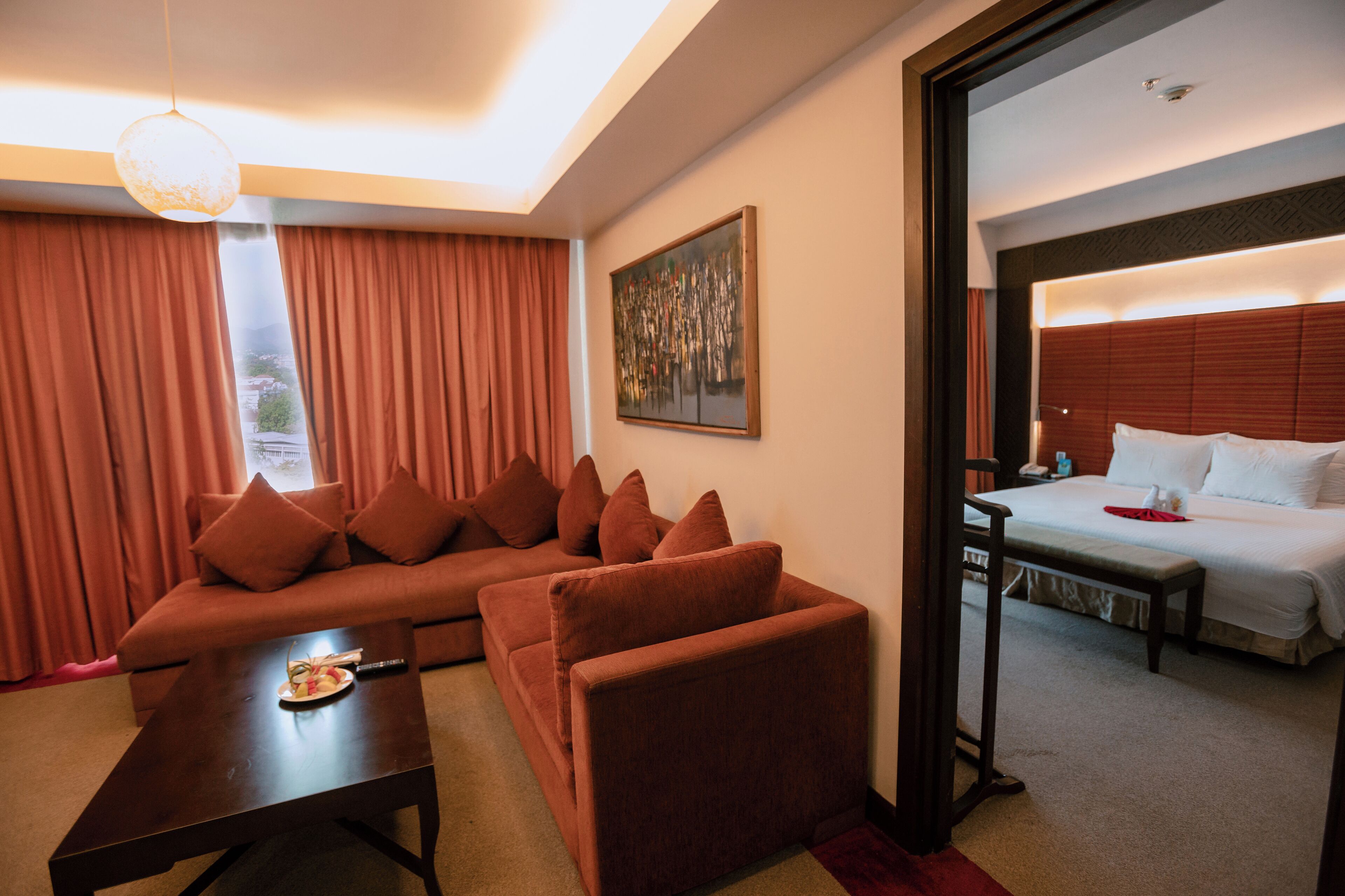 Quarto de hotel com sofá, cama, mesa de cabeceira e um quadro na parede.