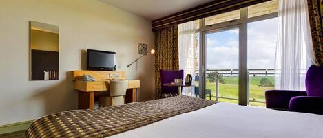 Quarto de hotel com uma cama grande, uma escrivaninha com televisão, uma cadeira e uma varanda com vista para o campo.
