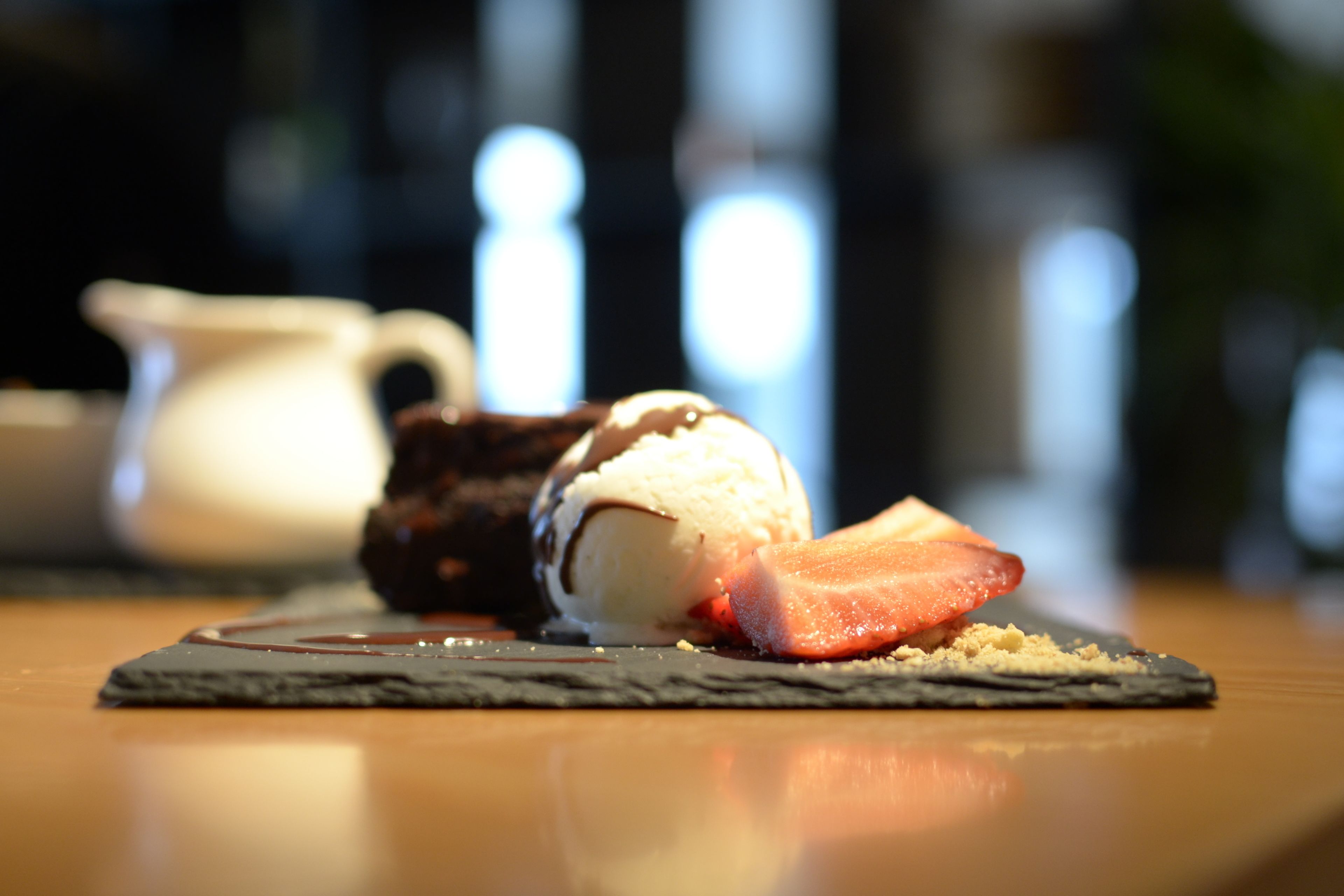 Sobremesa em um prato de ardósia com um sorvete de casquinha coberto de chocolate e uma fatia de morango.