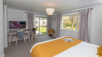 Quarto de hotel com cama, escrivaninha com cadeira, televisão e vista para o exterior.