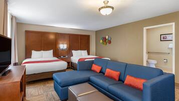 Quarto de hotel com duas camas, um sofá, uma televisão e um banheiro.