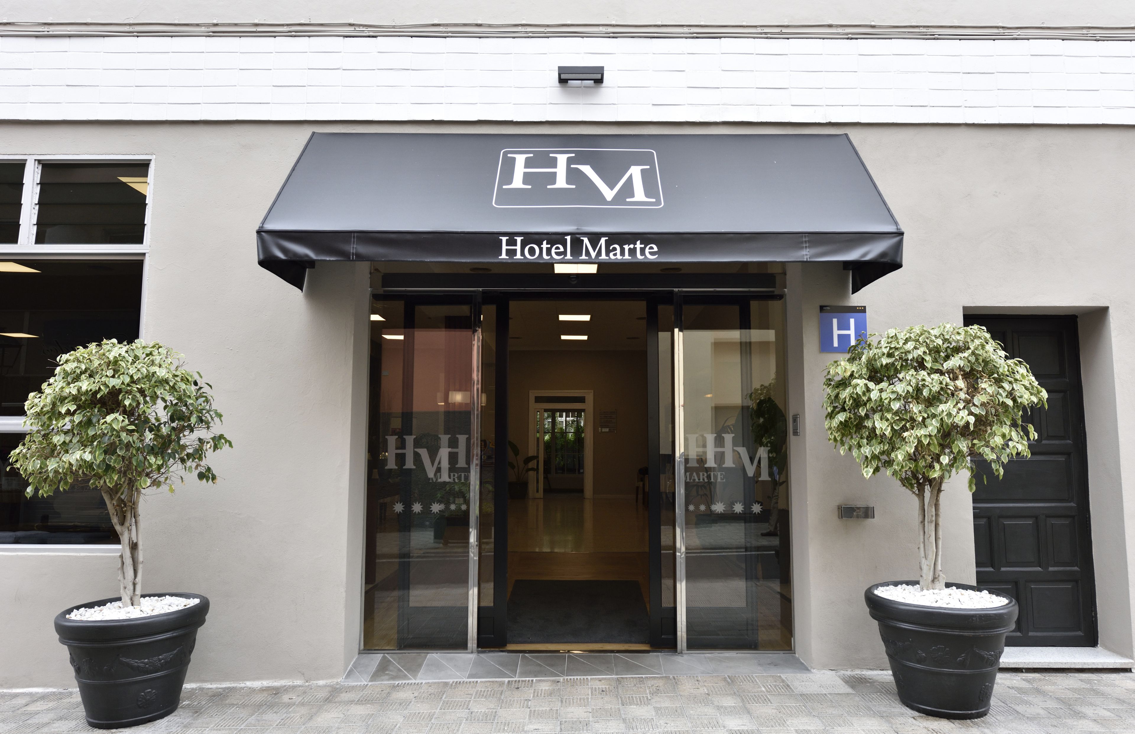 A entrada do Hotel Marte, com toldo preto exibindo o nome e o logotipo do hotel.