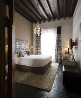 Quarto com cama grande, lustre, mesa de cabeceira e vista para o exterior.