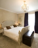 Quarto com uma cama grande, mesa de cabeceira, luminária, pintura e lustre.