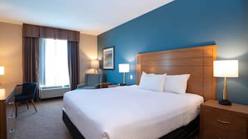 Quarto de hotel com uma cama grande, uma escrivaninha, uma cadeira e uma mesa de cabeceira com luminárias.