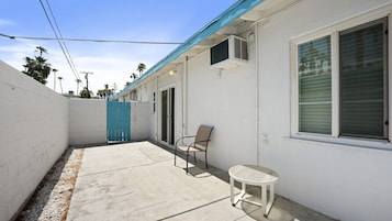 Um imóvel residencial com um pátio de concreto, uma porta azul, uma cadeira e uma pequena mesa.