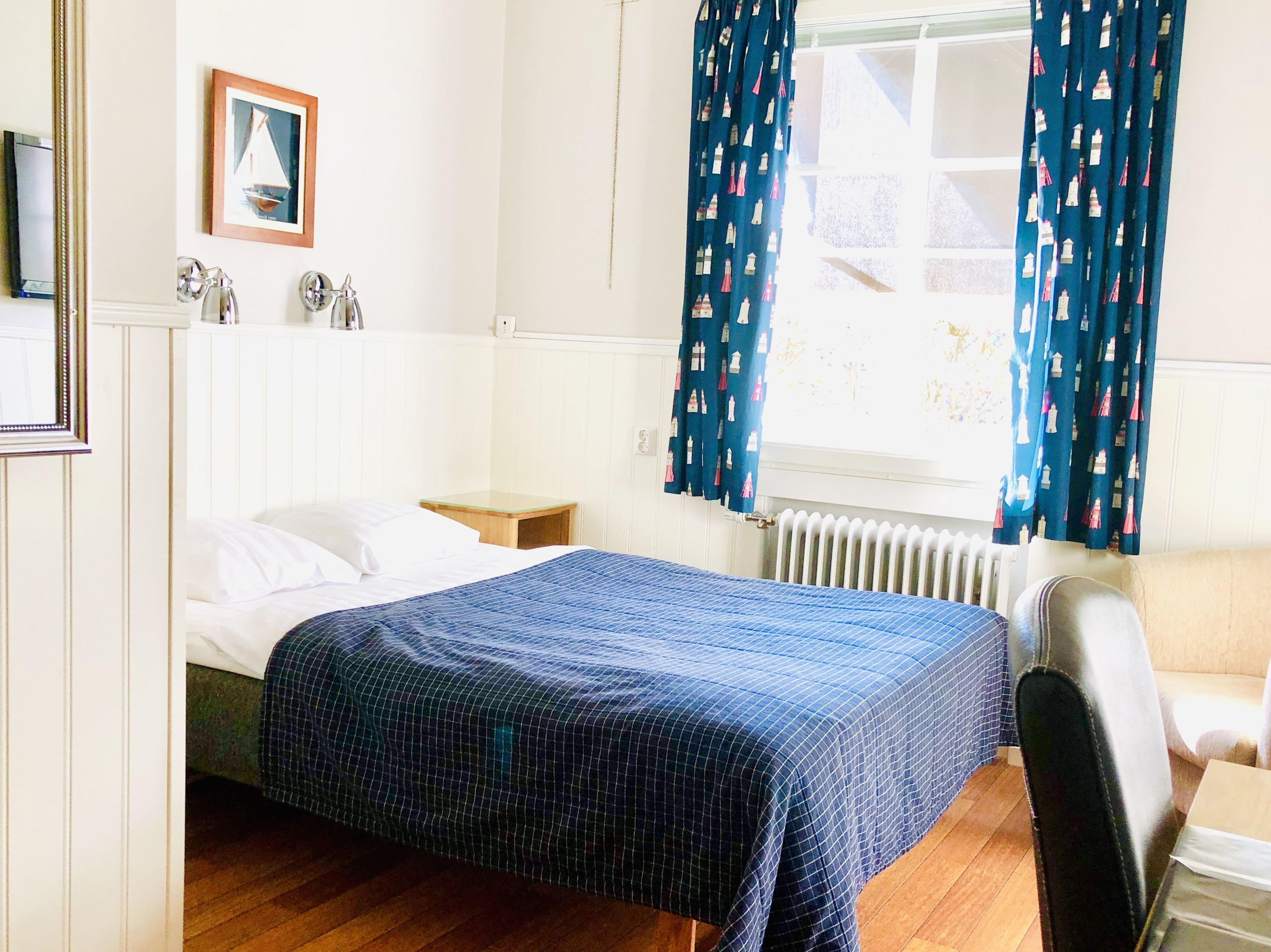 Quarto com cama, cadeira, mesinha, radiador e cortinas com padrão de farol.