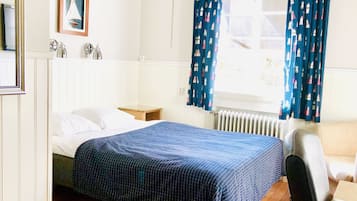 Quarto com cama, cadeira, mesinha, radiador e cortinas com padrão de farol.
