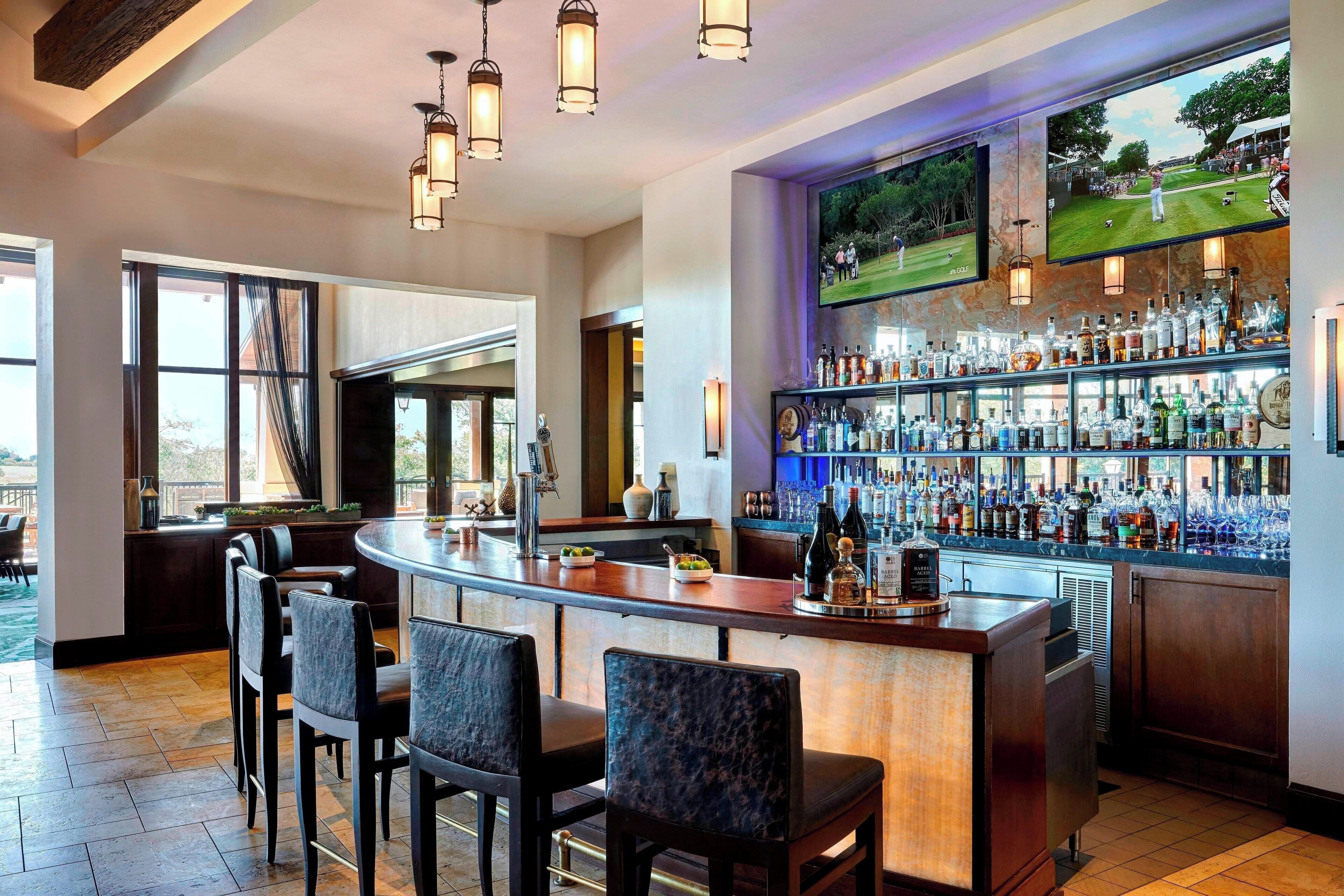Uma área de bar com balcão de madeira, vários bancos e uma variedade de bebidas.