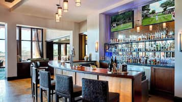 Uma área de bar com balcão de madeira, vários bancos e uma variedade de bebidas.