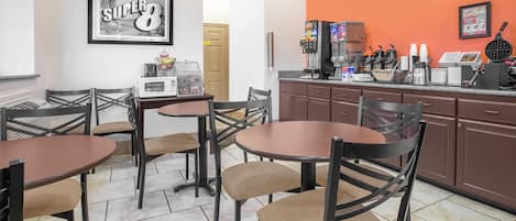 Interior de restaurante com mesas, cadeiras, uma máquina de café e um balcão com diversos itens.
