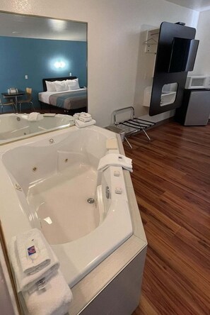 Quarto de hotel com uma banheira grande, uma cama, uma escrivaninha e um espelho.