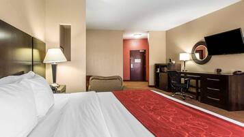 Quarto de hotel com cama grande, escrivaninha, cadeira, televisão e tapete vermelho.