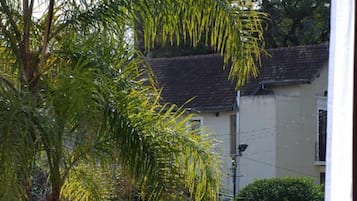 Uma varanda com mesa e cadeiras, dando vista para um jardim com palmeiras e um prédio ao fundo.