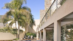 Uma área de piscina moderna com deck de madeira e borda de pedras, cercada por edifícios com elementos de pedra e vidro.