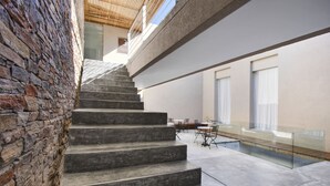 Um interior moderno com uma parede de pedra, uma escadaria e um guarda-corpo de vidro com vista para um pátio.