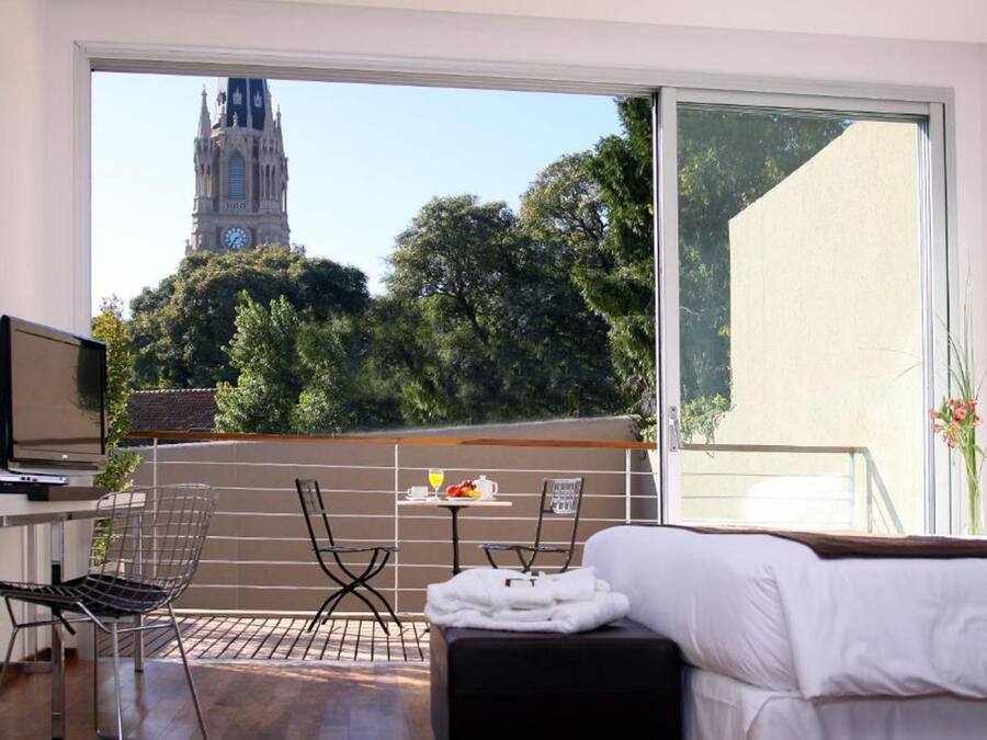 Uma varanda com um laptop, duas cadeiras, uma mesa pequena com um copo de suco e vista para uma torre.